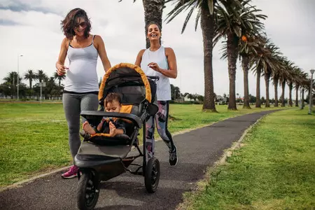 Buntis na tumatakbo kasama ang sanggol sa isang pushchair