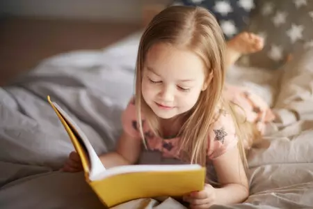 Bliska portret małej dziewczynki czytającej w łóżku
