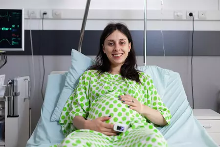 Portret kobiety w ciąży siedzącej na oddziale szpitalnym na łóżku